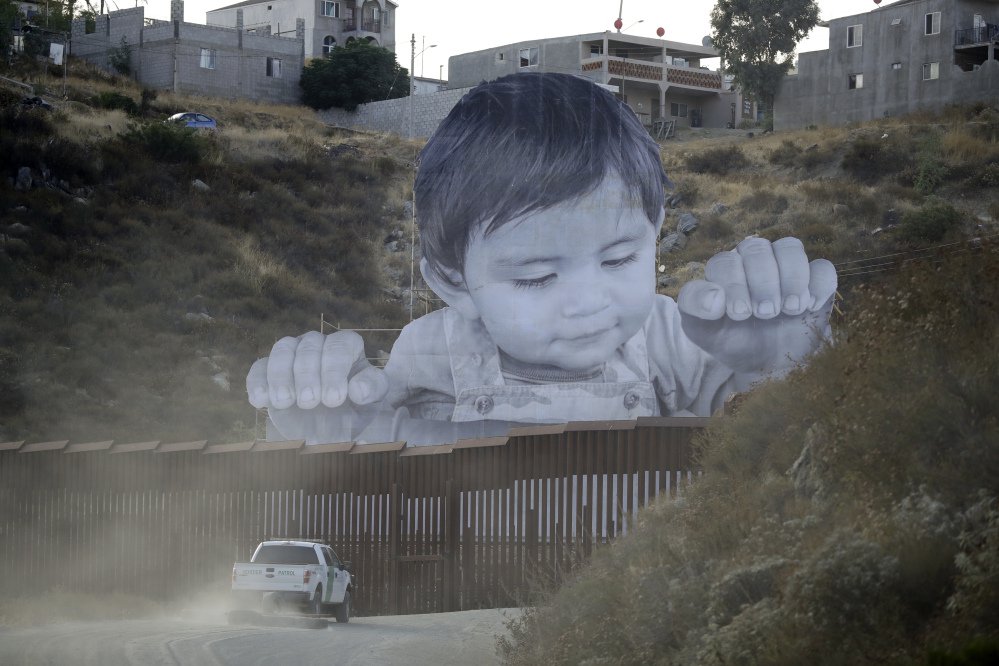 Towering photo of boy peers over Mexican border wall